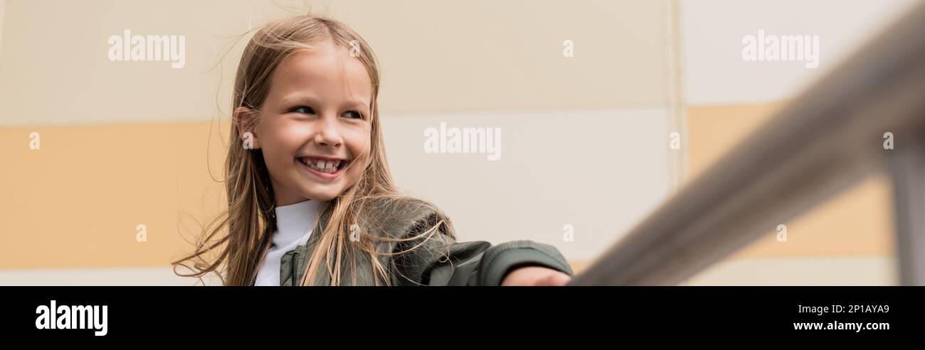 joyful preteen girl in stylish bomber jacket leaning on metallic ...