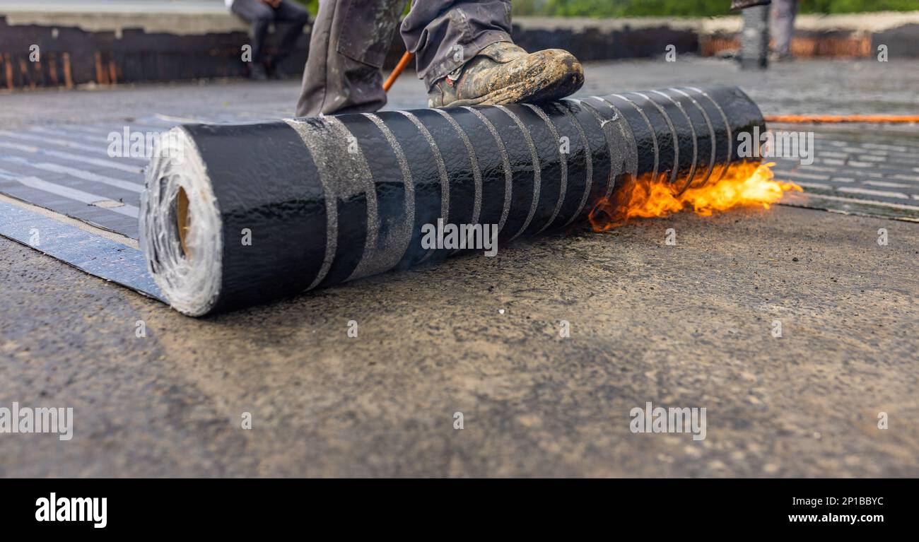 Workers placing a vapor barrier on the roof using a propane gas torch ...