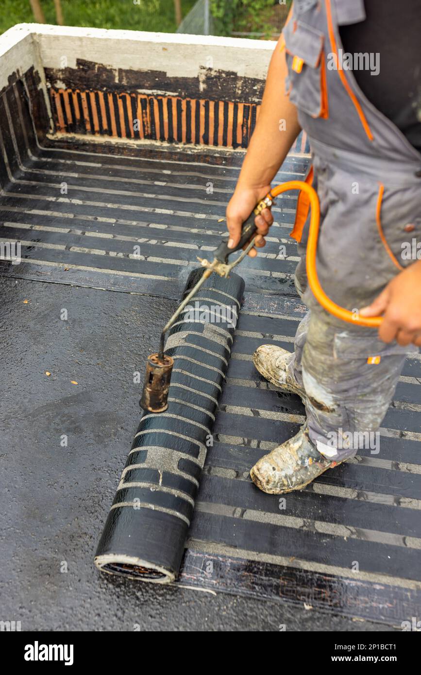 Workers placing a vapor barrier on the roof using a propane gas torch ...