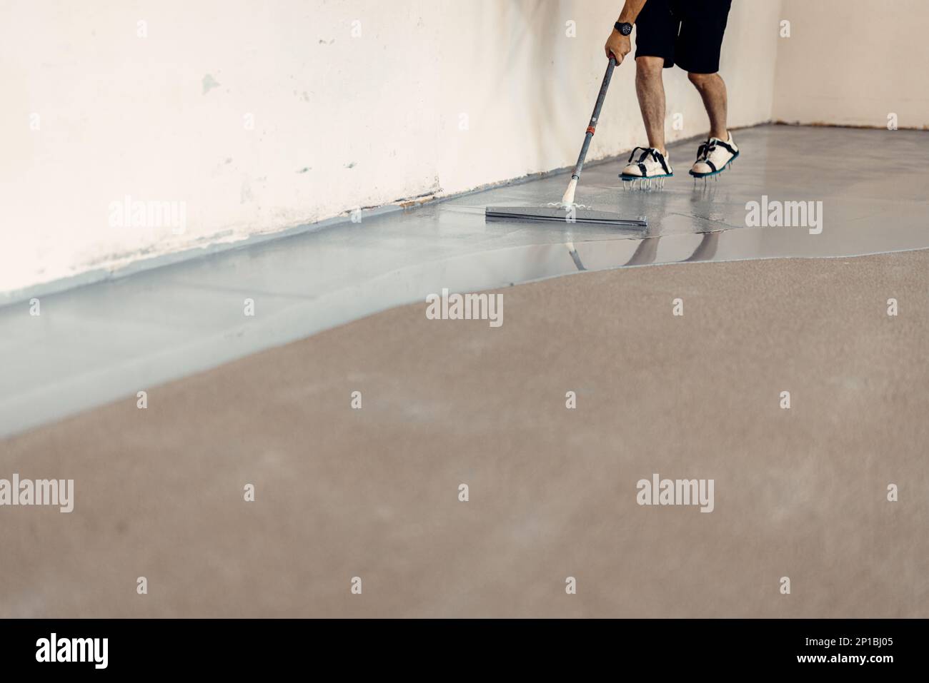 A construction worker apply grey epoxy resin in an industrial hall ...