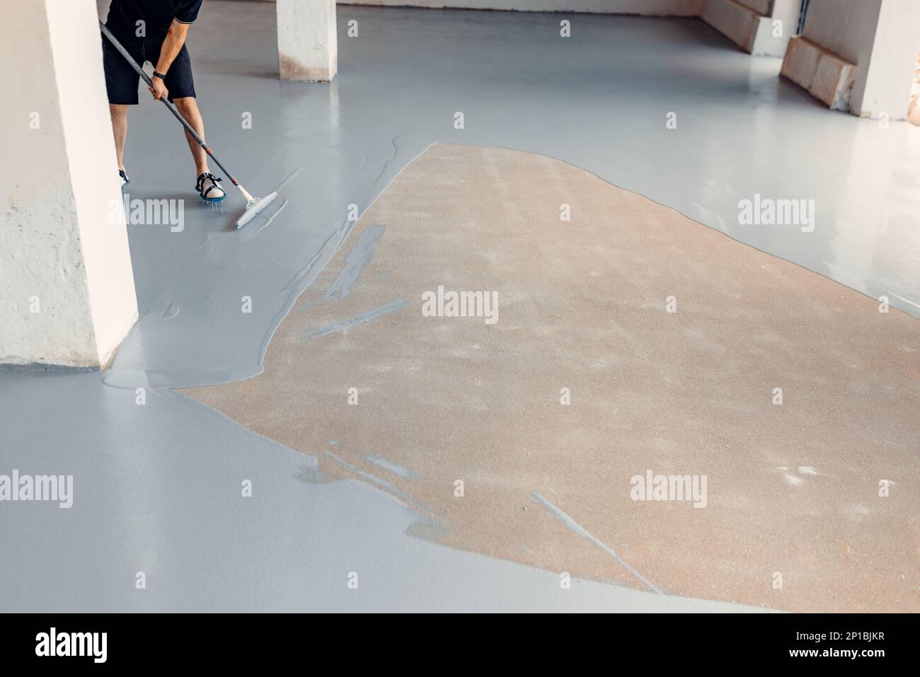 A construction worker apply grey epoxy resin in an industrial hall ...