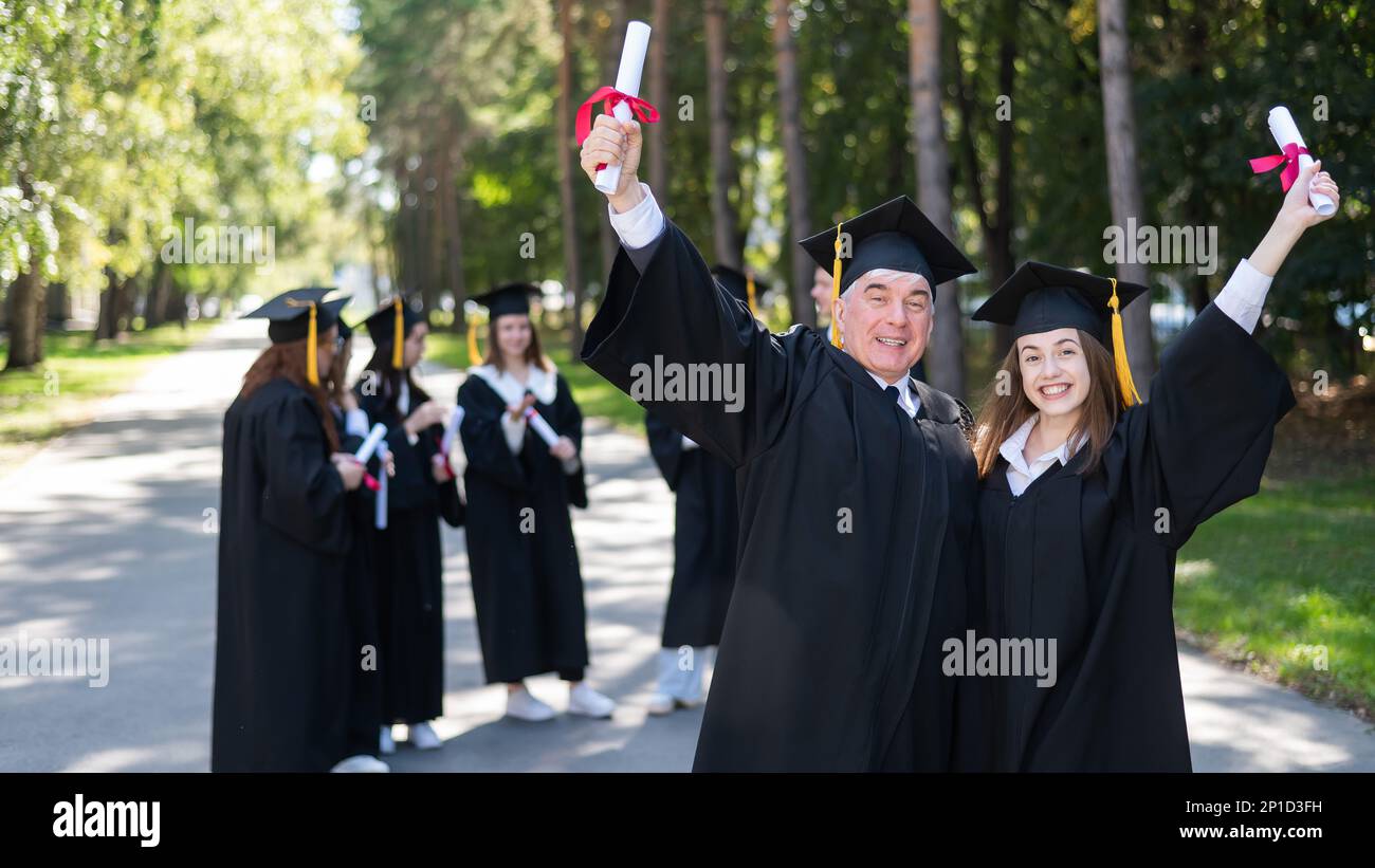 A group of graduates in robes outdoors. An elderly man and a young ...