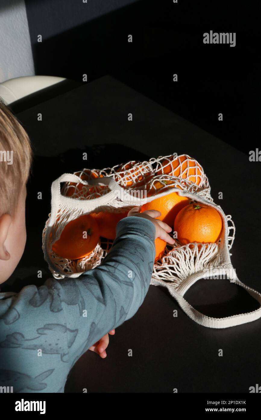 little kid grabbing oranges from mesh bag, dark background Stock Photo ...