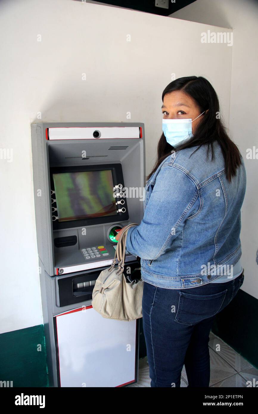 Latin woman with protection mask clinical use in ATM withdrawing money ...