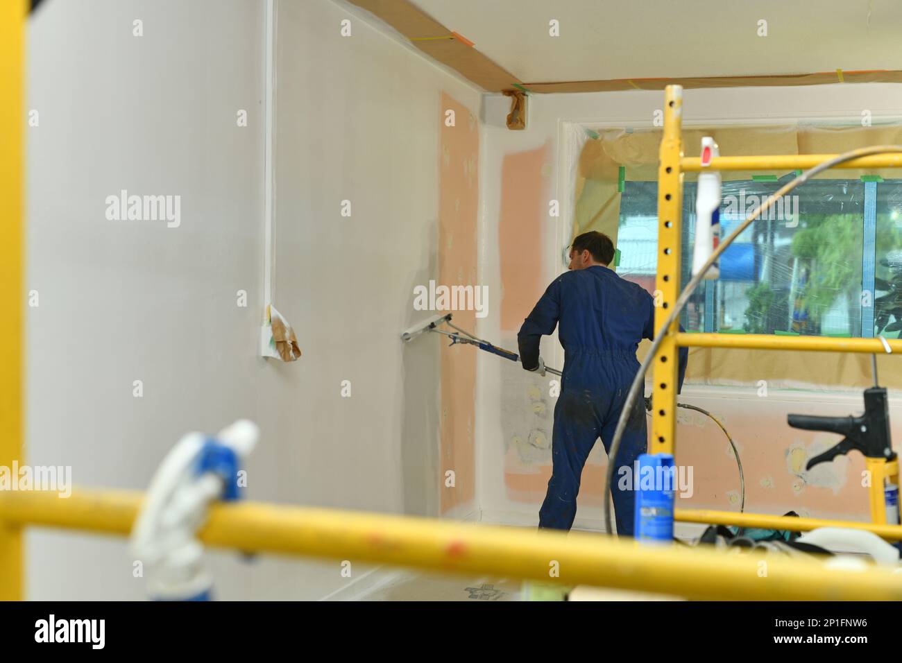 A painter applies an acrylic primer coat to the interior walls of a ...