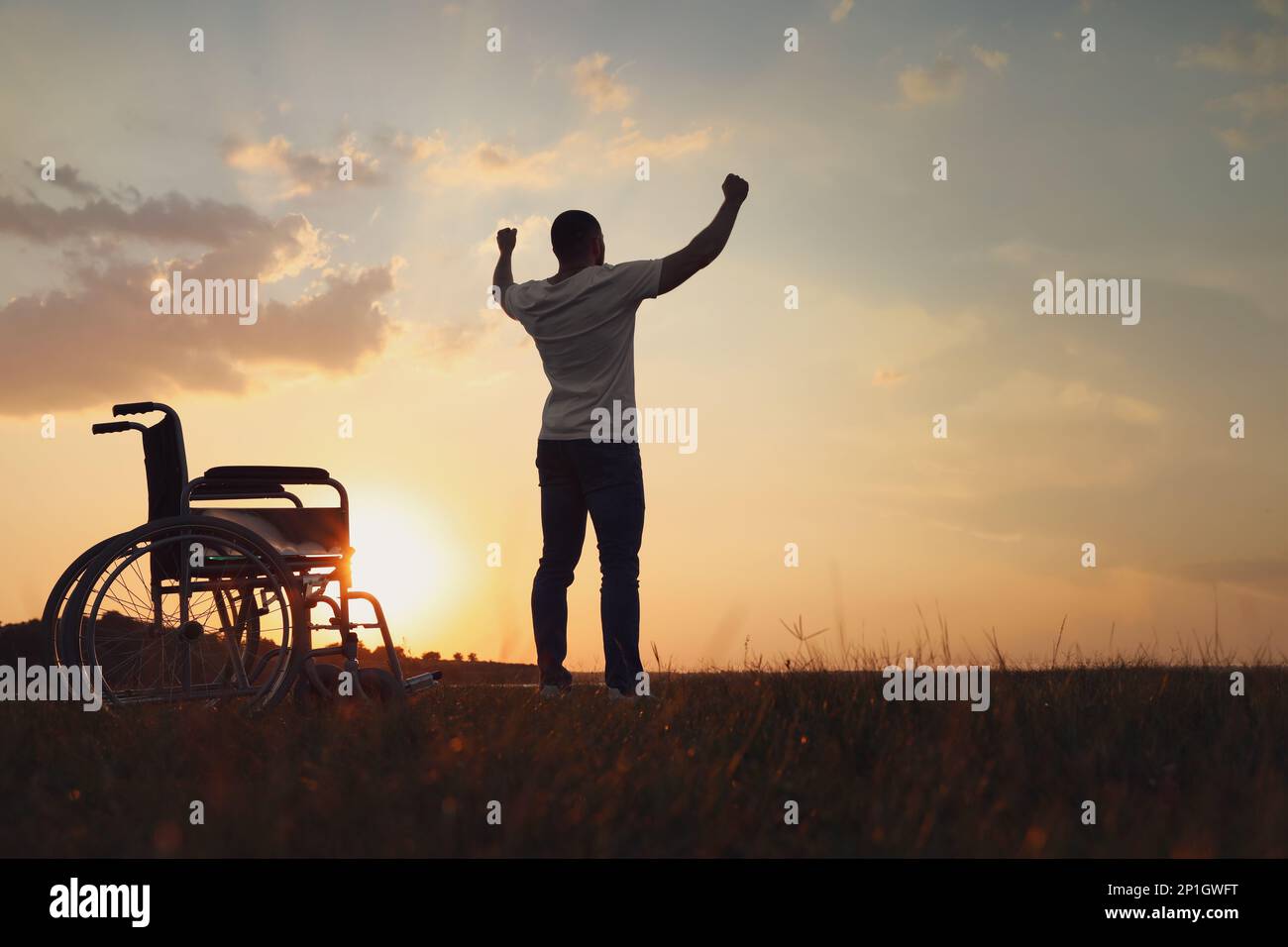Man raising hands up to sky near wheelchair at sunset, back view ...