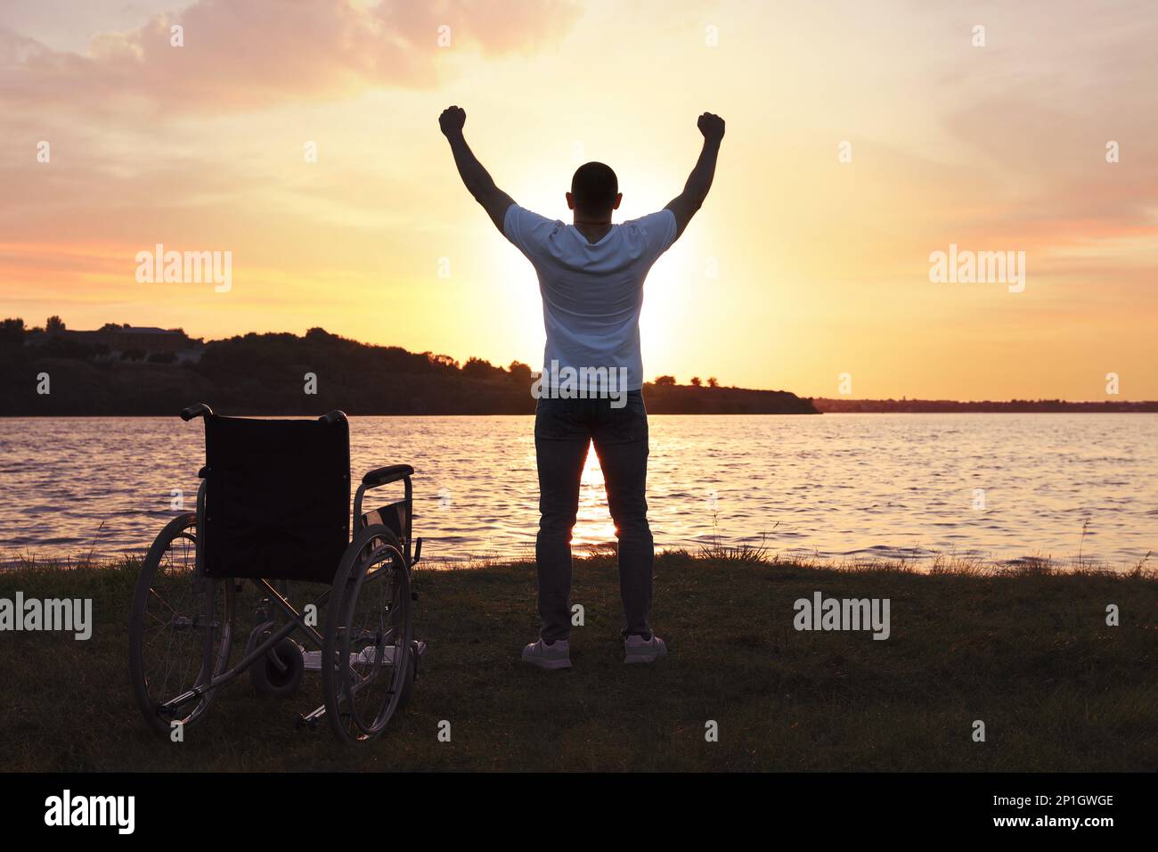 Man raising hands up to sky near wheelchair at sunset, back view ...