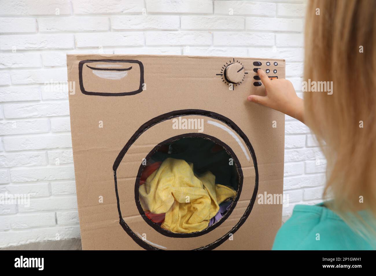 Little girl playing with toy cardboard washing machine indoors, closeup ...