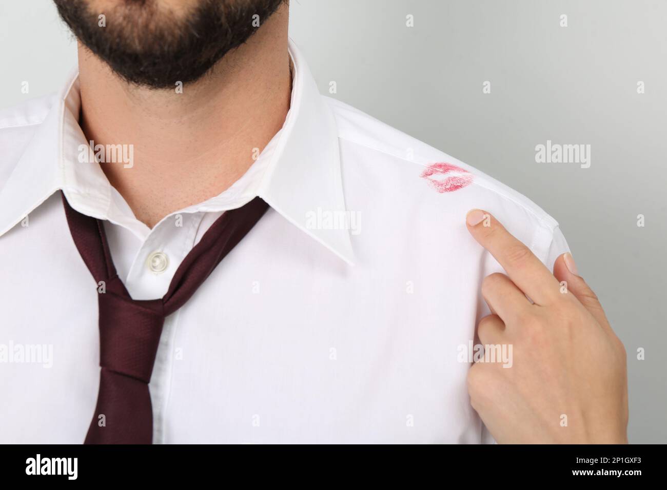 Woman pointing at lipstick kiss mark on her husband's shirt, closeup ...