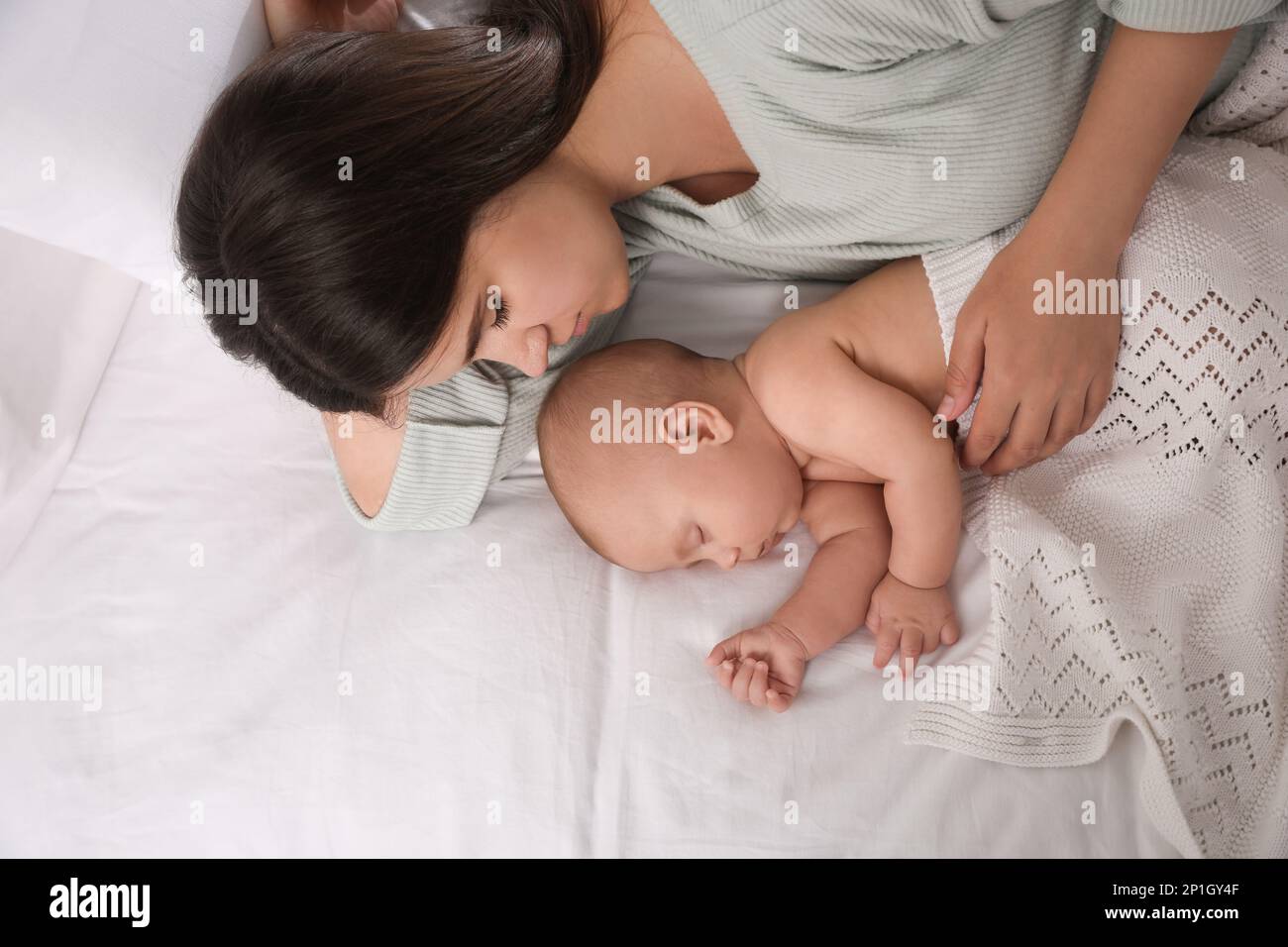 Young mother resting near her sleeping baby on bed, top view Stock ...