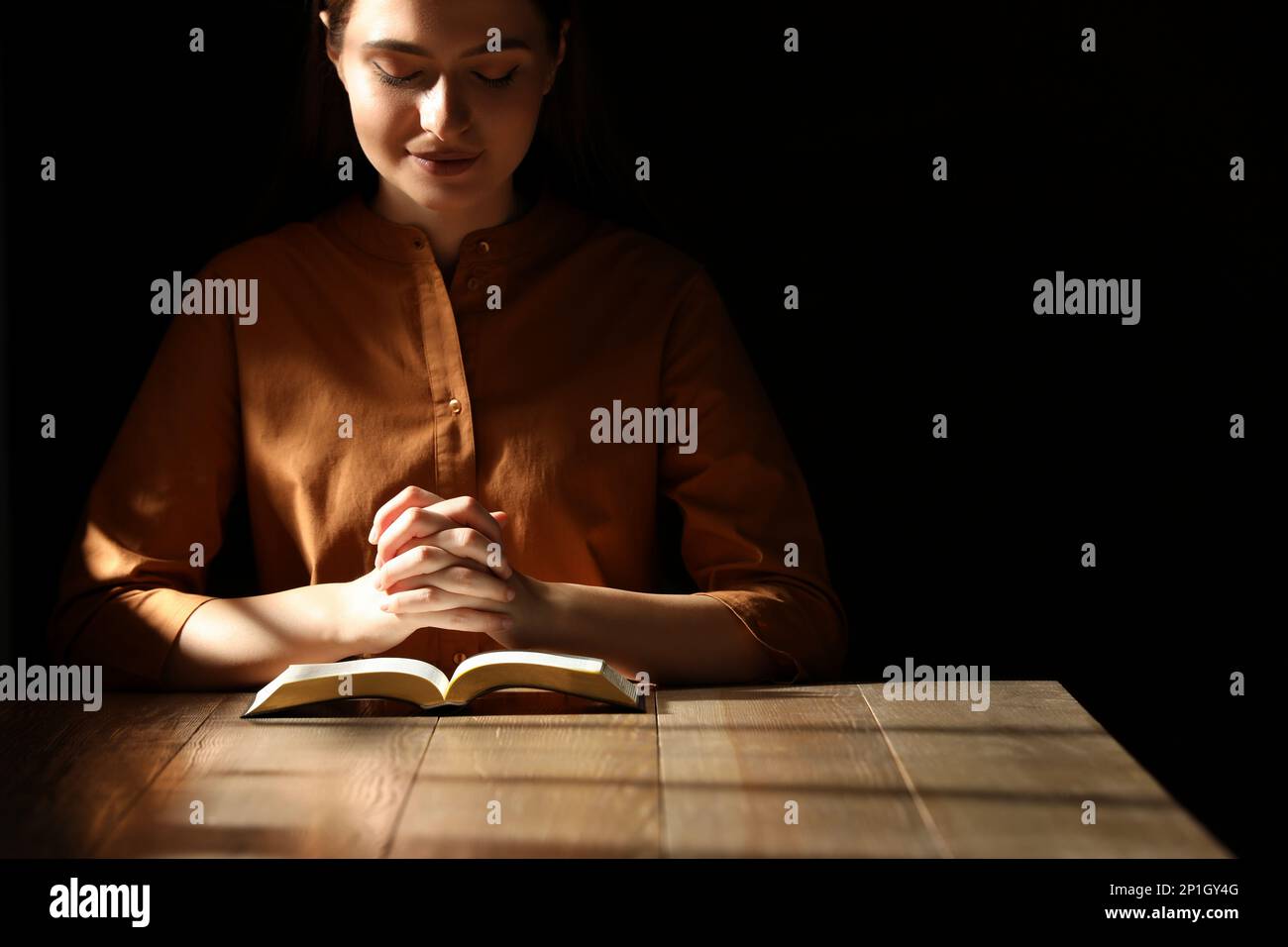 Religious young woman praying over Bible at wooden table indoors Stock ...