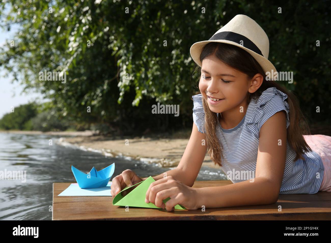 Cute little girl making paper boats on wooden pier near river Stock ...