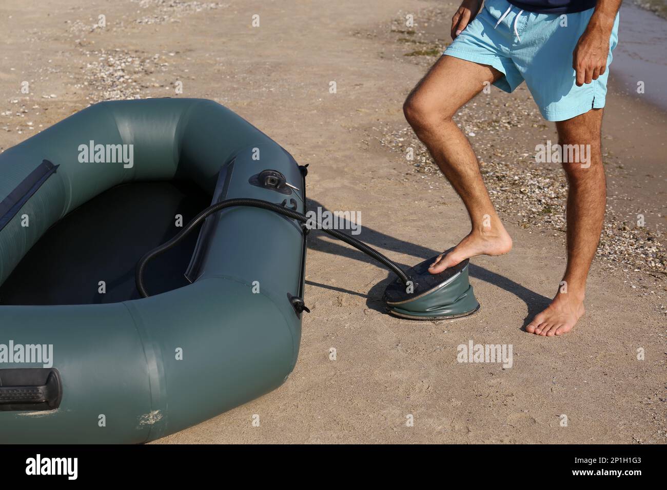 Man pumping inflatable rubber fishing boat at sandy beach on sunny day ...