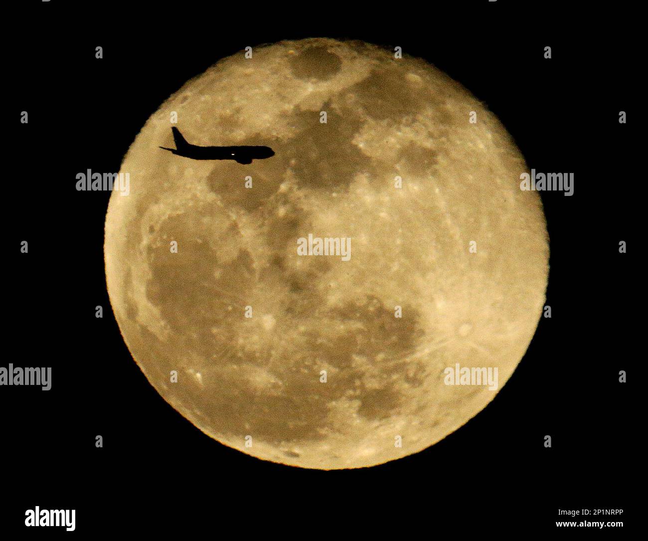 A passenger jet passes in front of the waning full moon as it ...