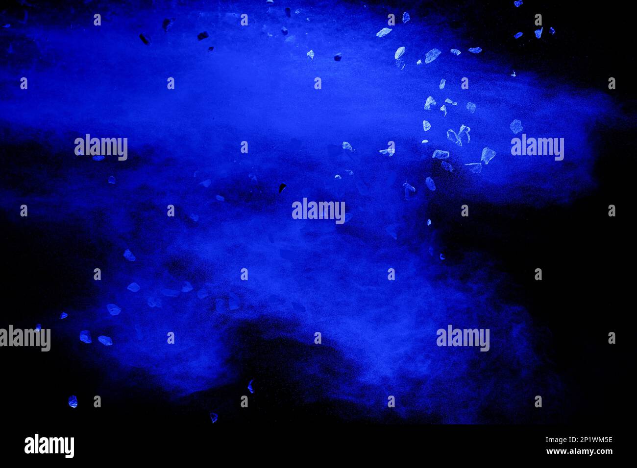 Split debris of stone exploding with blue powder against black ...