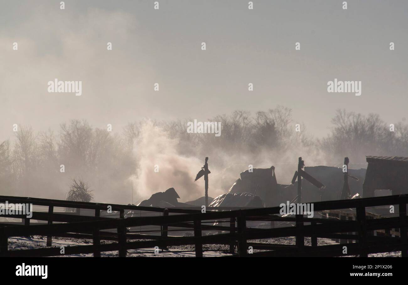 A barn destroyed by a fire stands with smoke at Classy Lane Stables ...