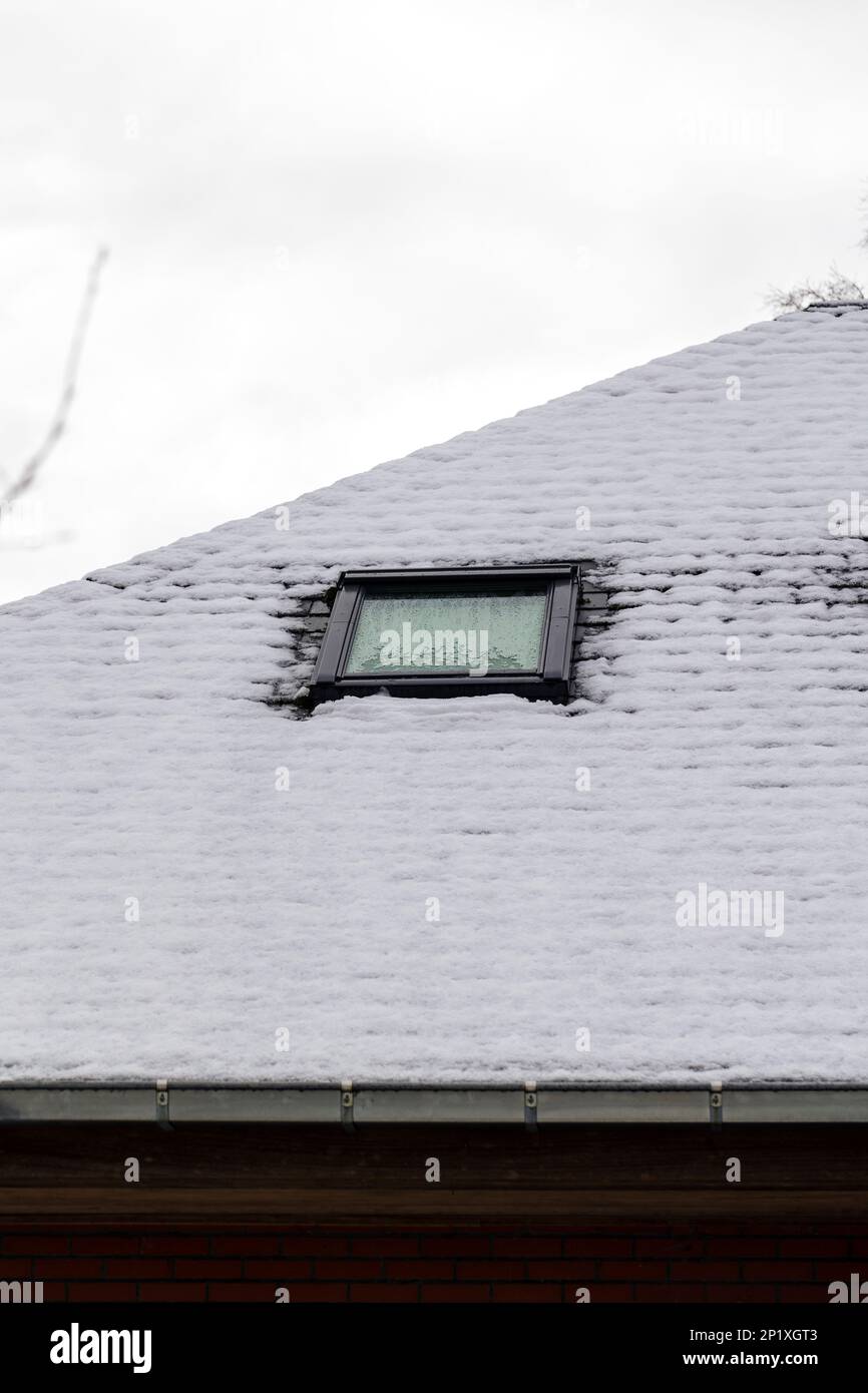 A portrait of a slate roof with snow on it with a skylight window which ...