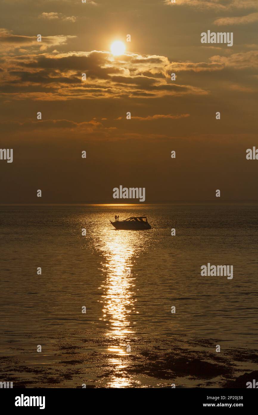 Boat in silhouette with a bright streak of sunlight going across the ...