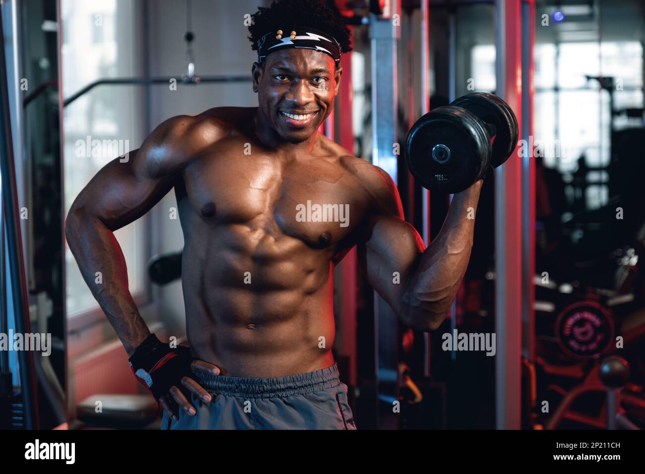 20s Black and muscular man in a gym doing biceps curl with a dumbbell ...