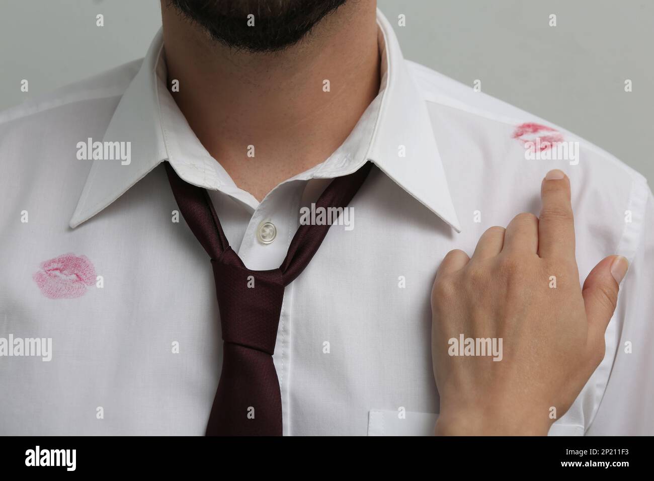 Woman pointing at lipstick kiss mark on her husband's shirt, closeup ...