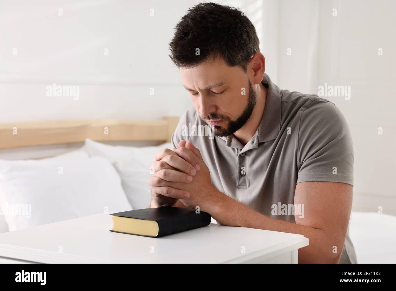 Religious man with Bible praying in bedroom Stock Photo - Alamy