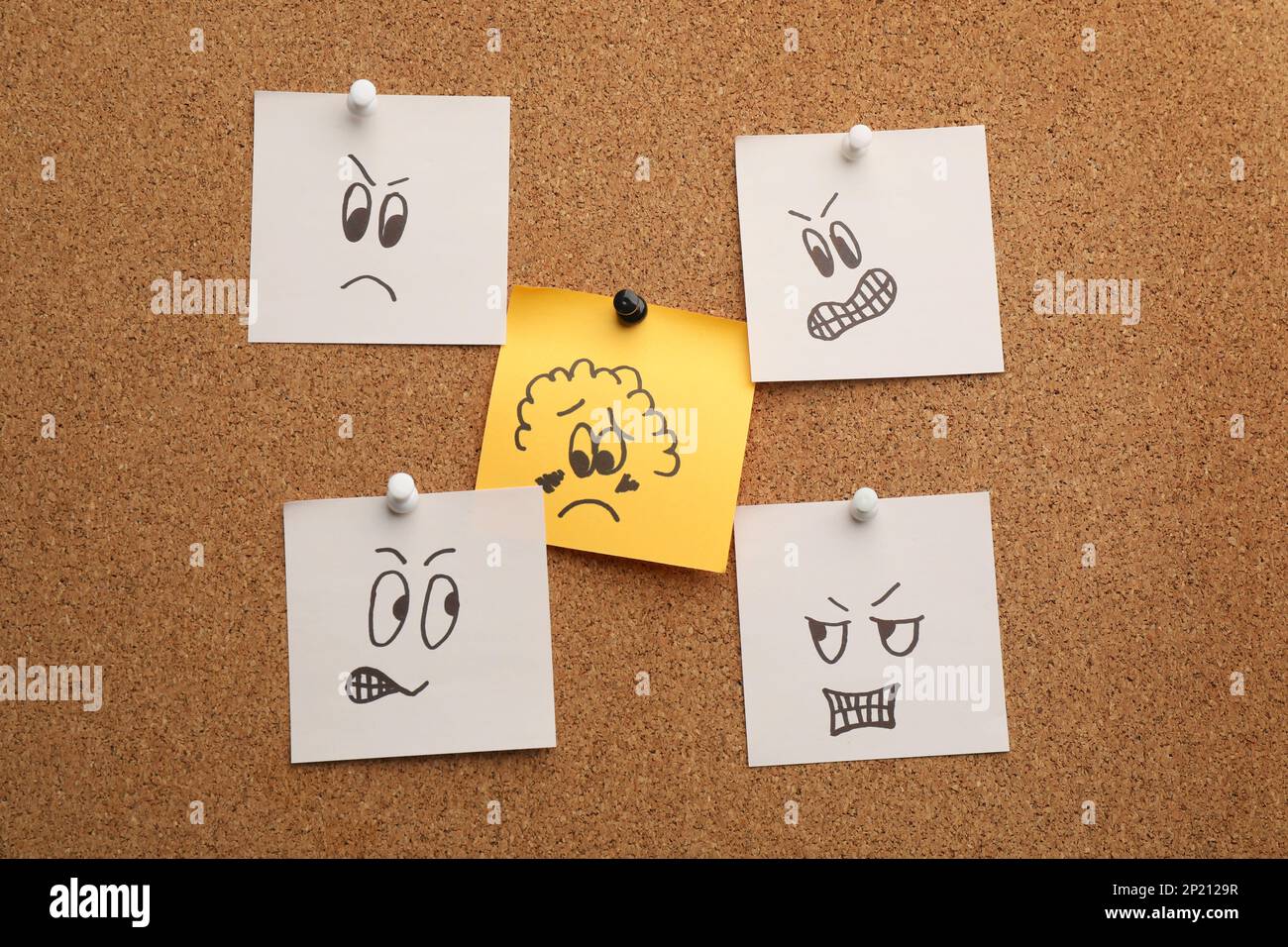 Yellow paper note with drawn sad face among aggressive ones pinned to ...