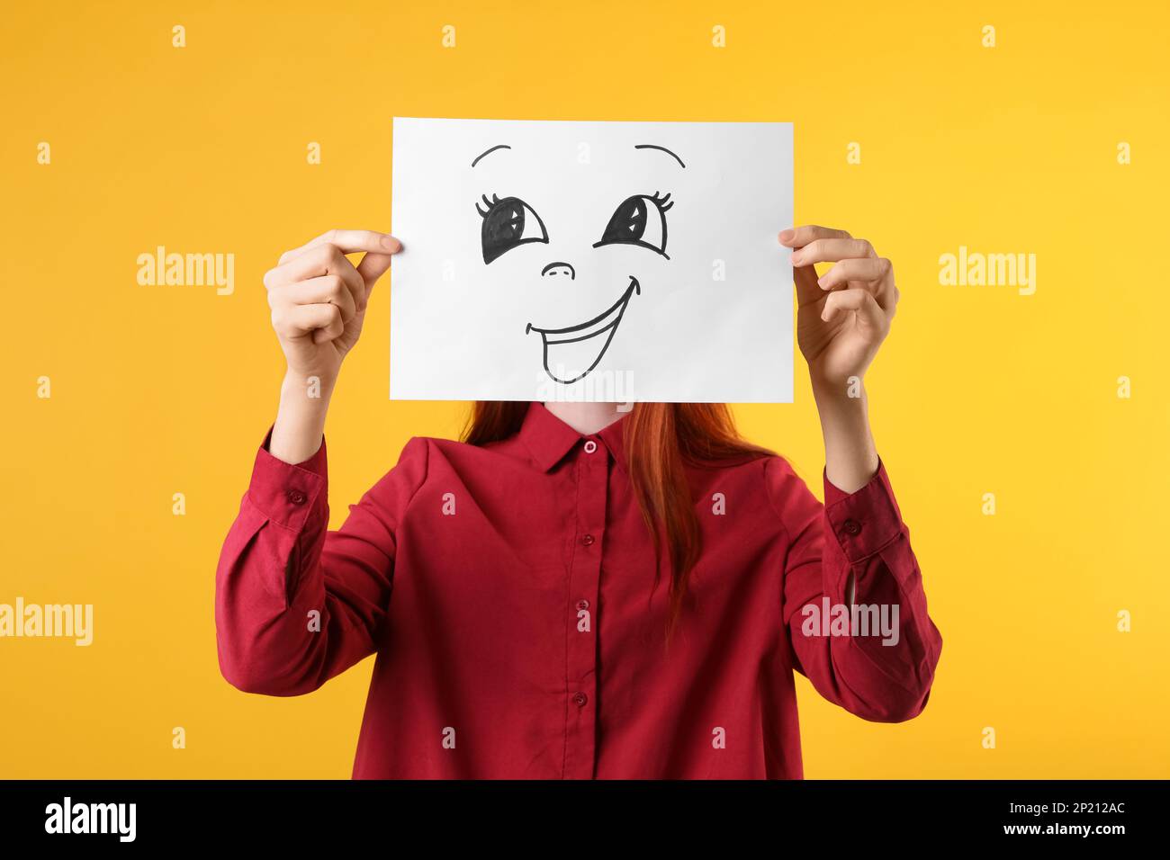 Woman hiding behind sheet of paper with happy face on yellow background ...