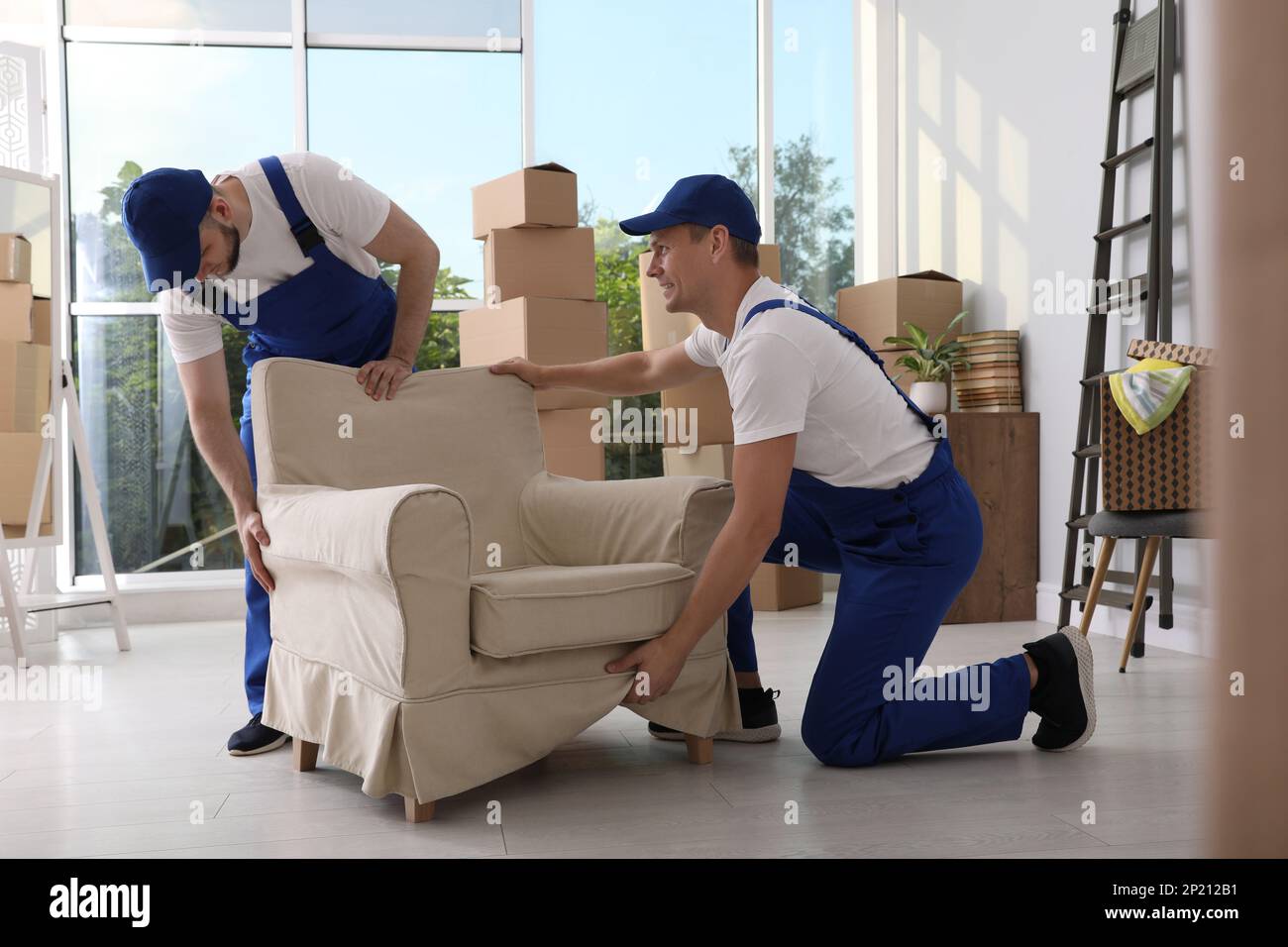 Moving service employees carrying armchair in room Stock Photo - Alamy