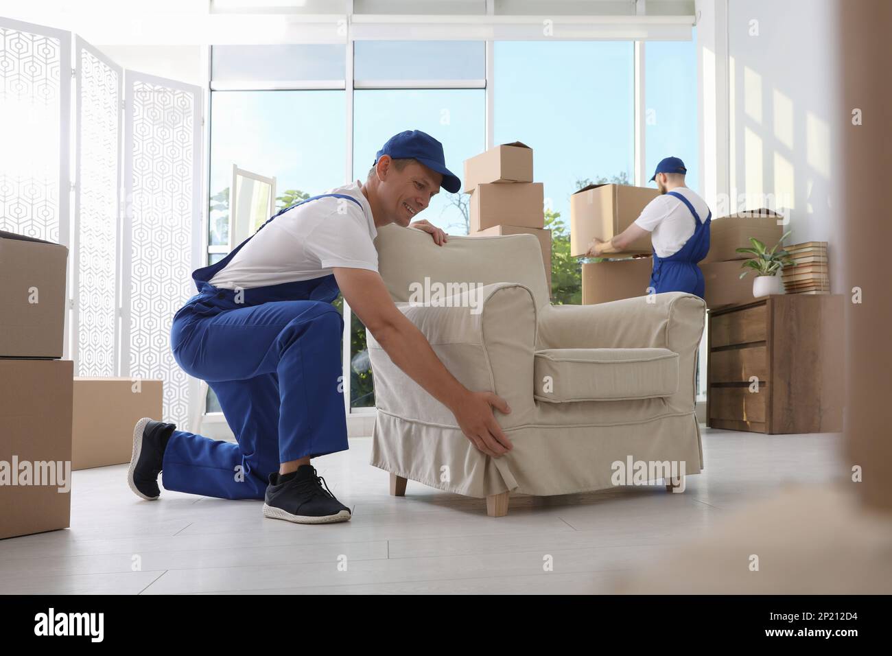 Moving service employees with armchair and cardboard boxes in room ...