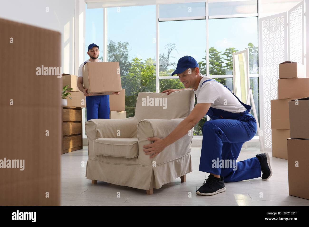 Moving service employees with armchair and cardboard boxes in room ...