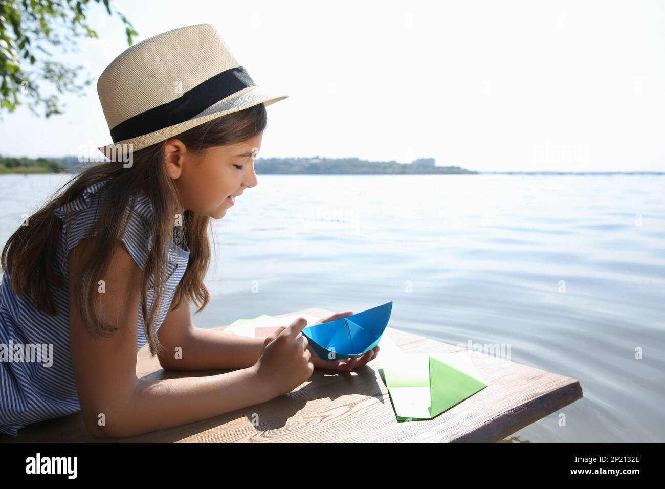 Cute little girl making paper boats on wooden pier near river Stock ...