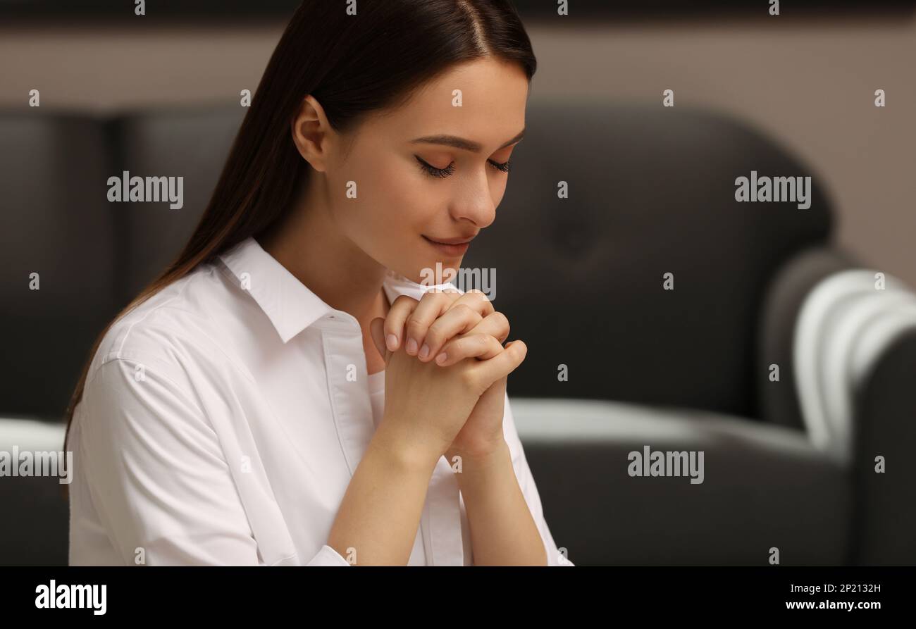 Religious young woman with clasped hands praying indoors Stock Photo ...