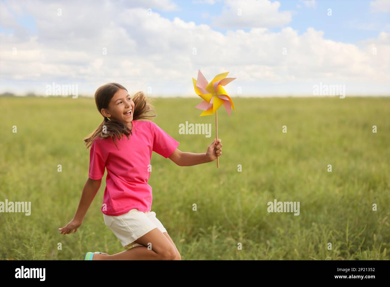 Cute little girl with pinwheel in field, space for text. Child spending ...