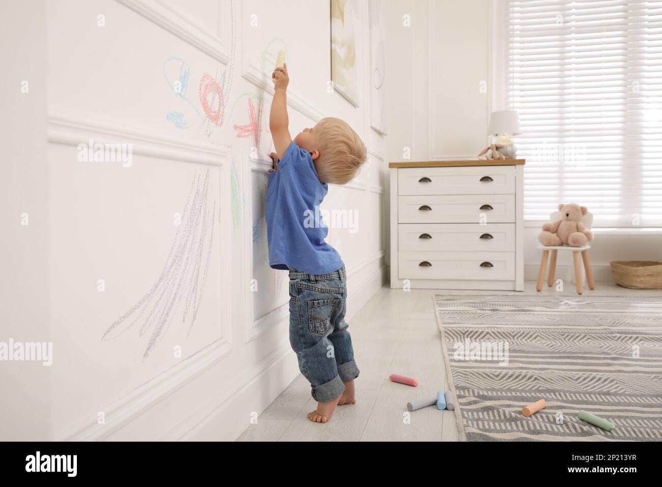 Mischievous little boy drawing with colorful chalk on white wall at ...