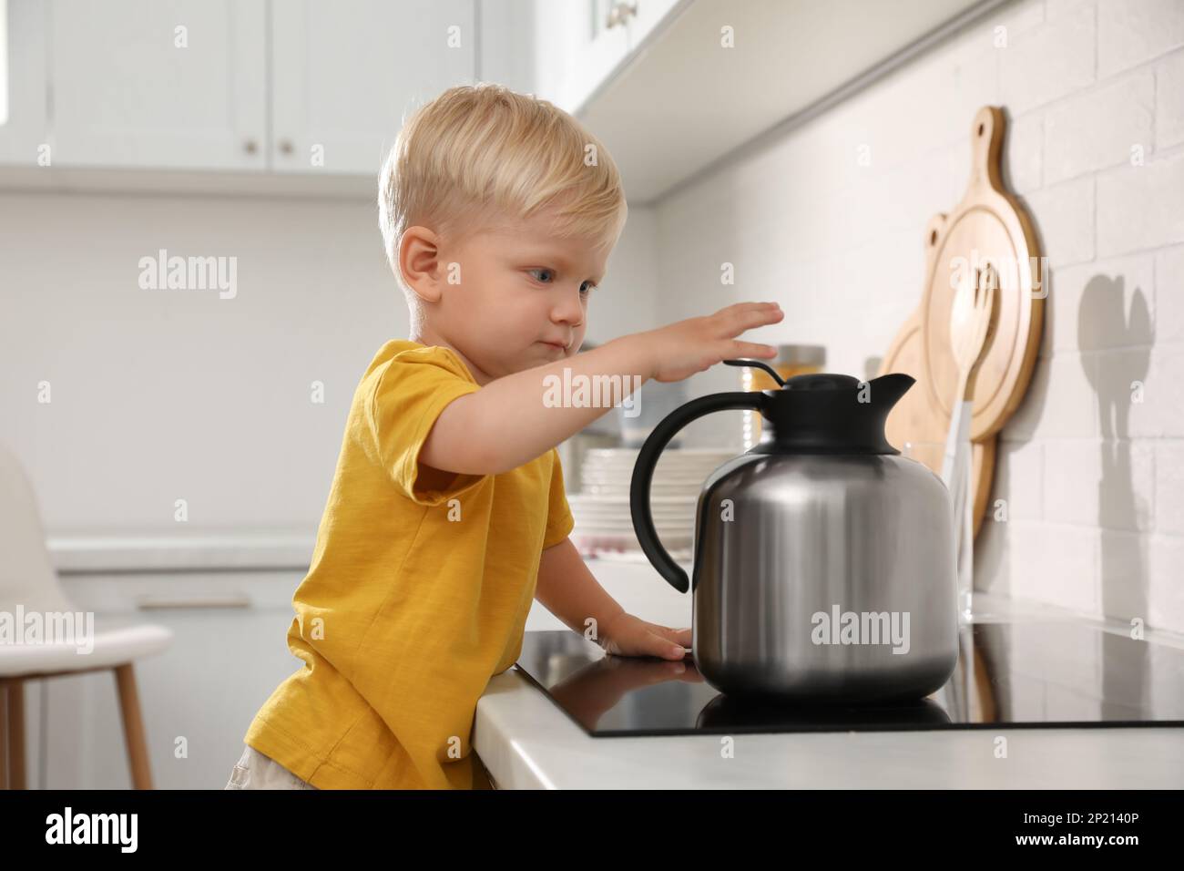 Curious little boy playing with kettle on electric stove in kitchen ...