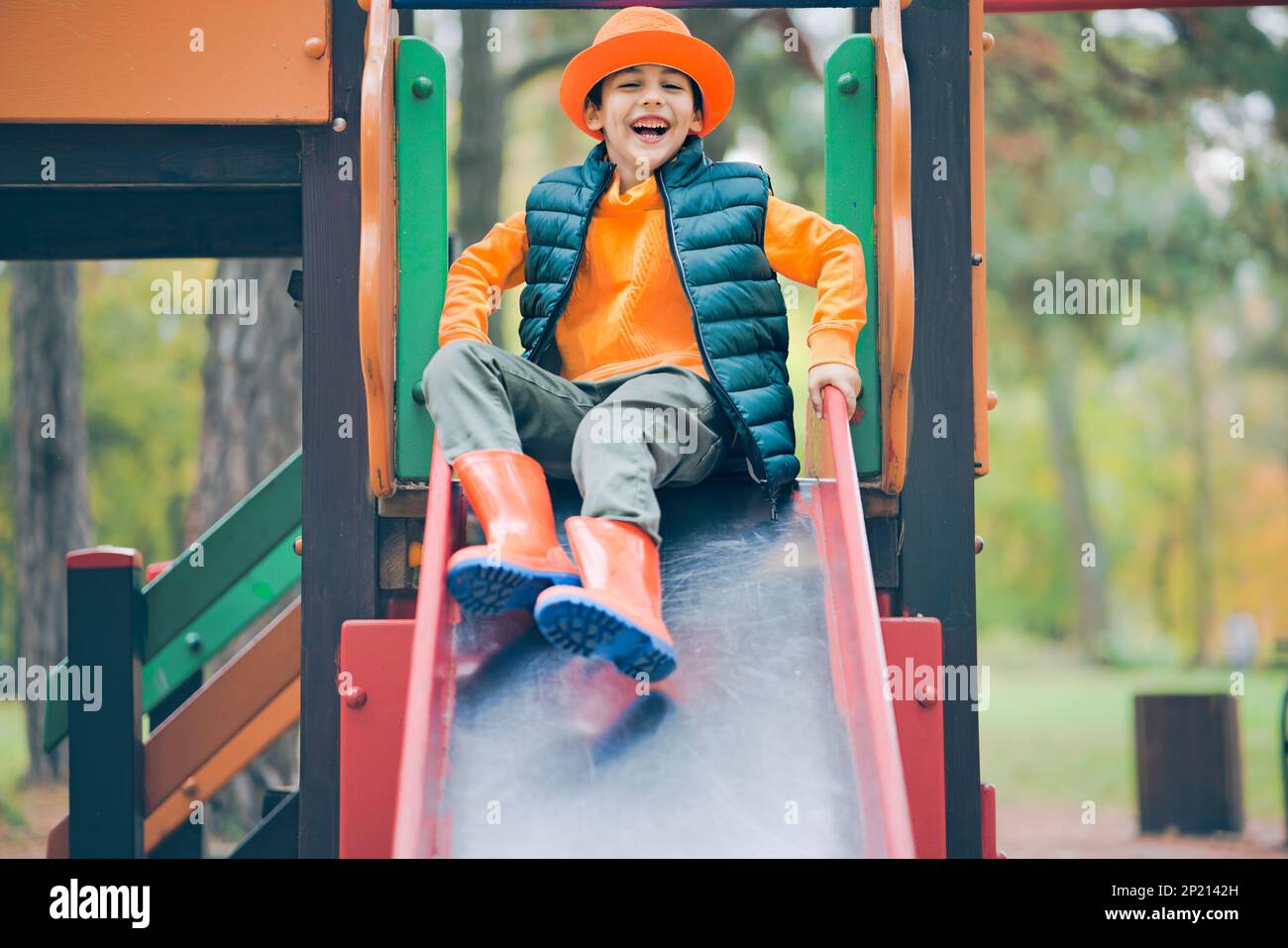 Happy little boy slides down the slide at the children's playground ...
