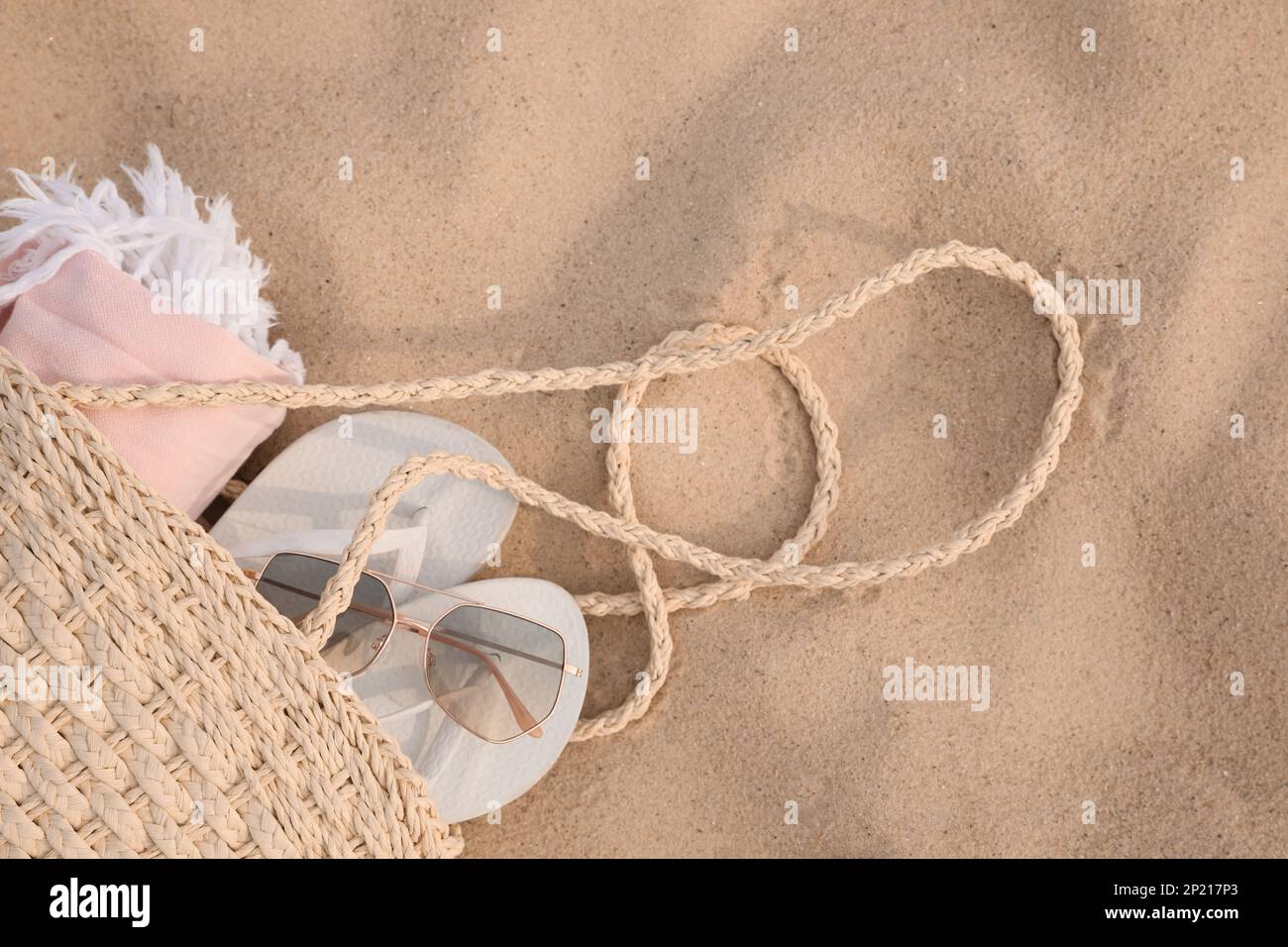 Beach bag with flip flops, towel and sunglasses on sand, top view ...
