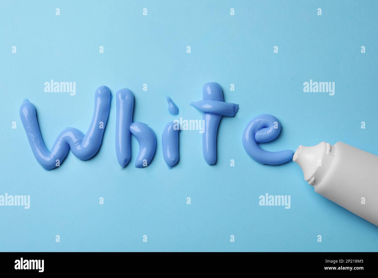 Word White written with toothpaste and tube on light blue background ...
