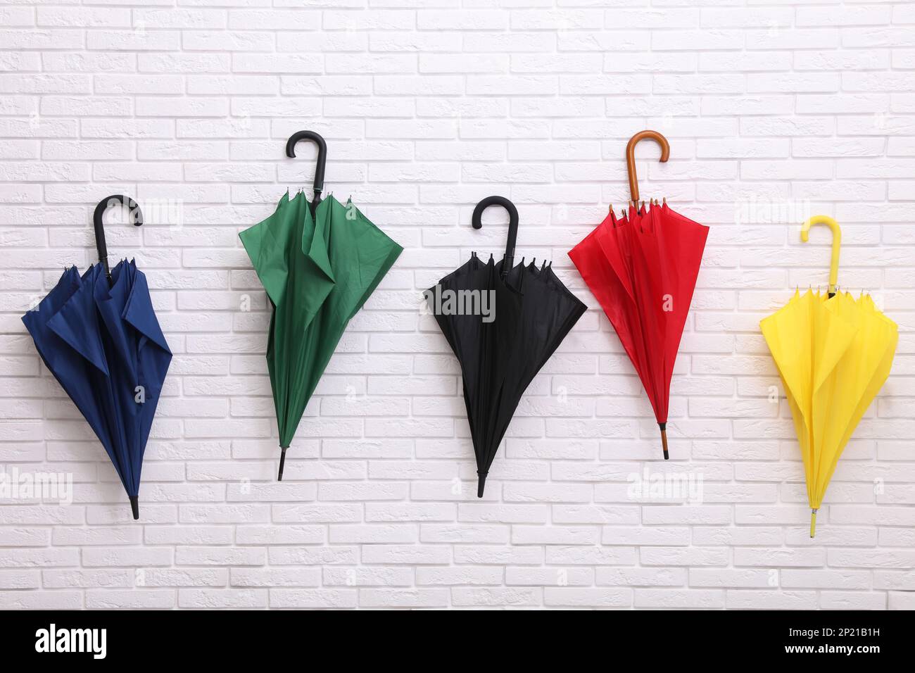 Closed bright umbrellas hanging on white brick wall Stock Photo - Alamy