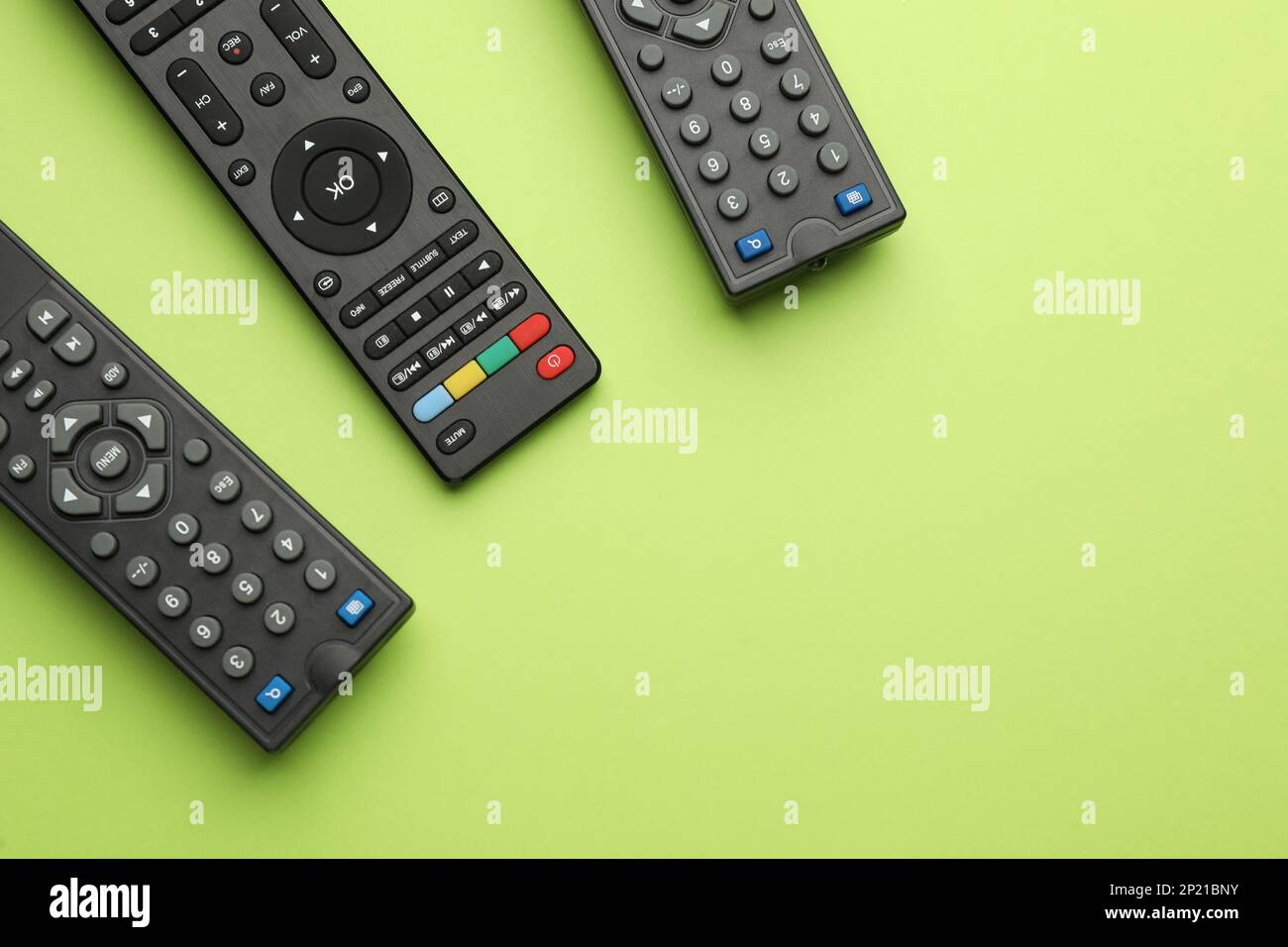 Remote controls on light green background, flat lay. Space for text ...