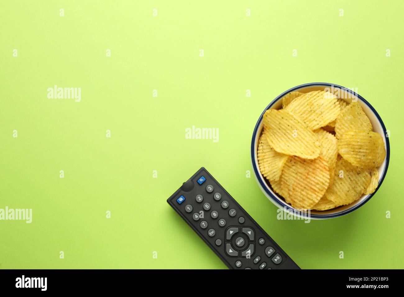 Remote control and bowl of potato chips on light green background, flat ...