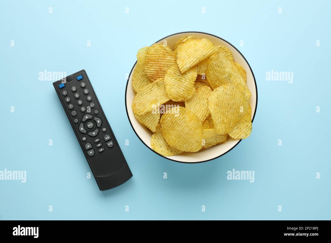Remote control and bowl of potato chips on light blue background, flat ...