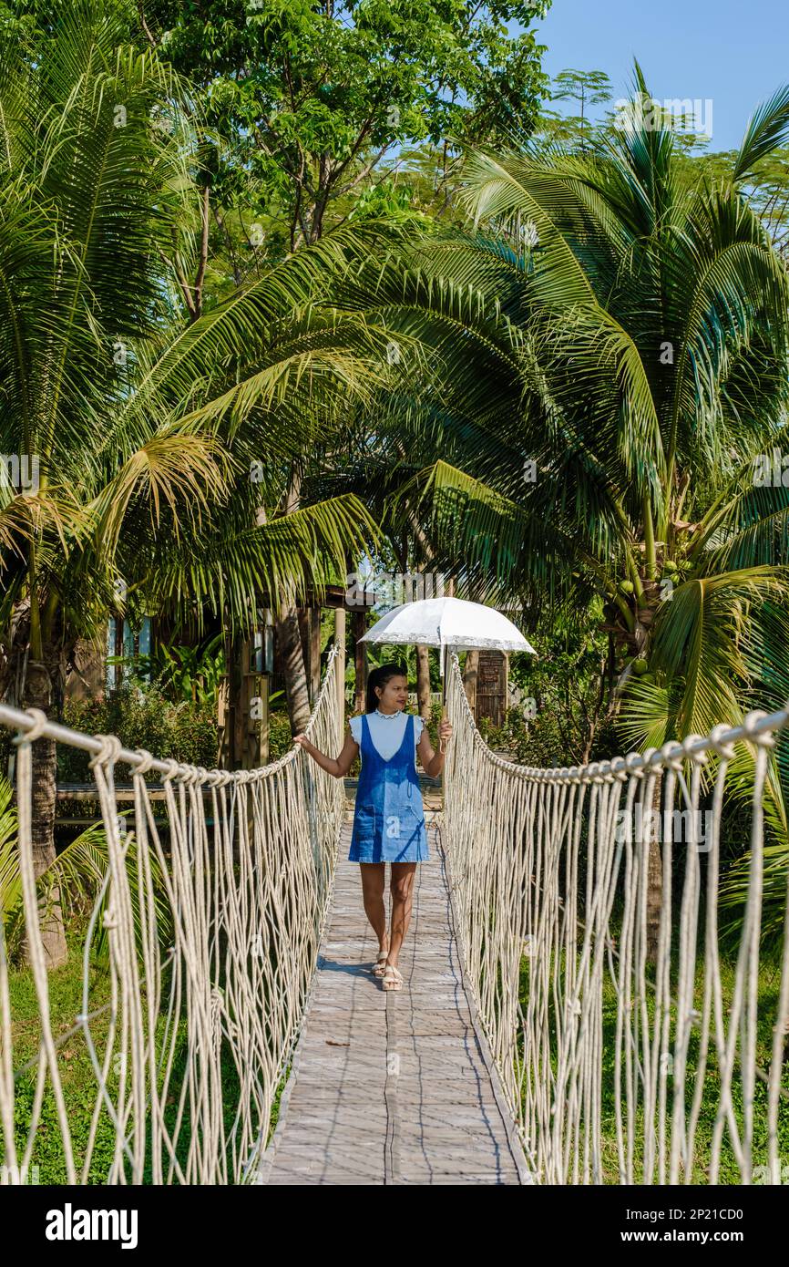 Asian women walking at a wooden bamboo rope bridge in the rainforest of ...