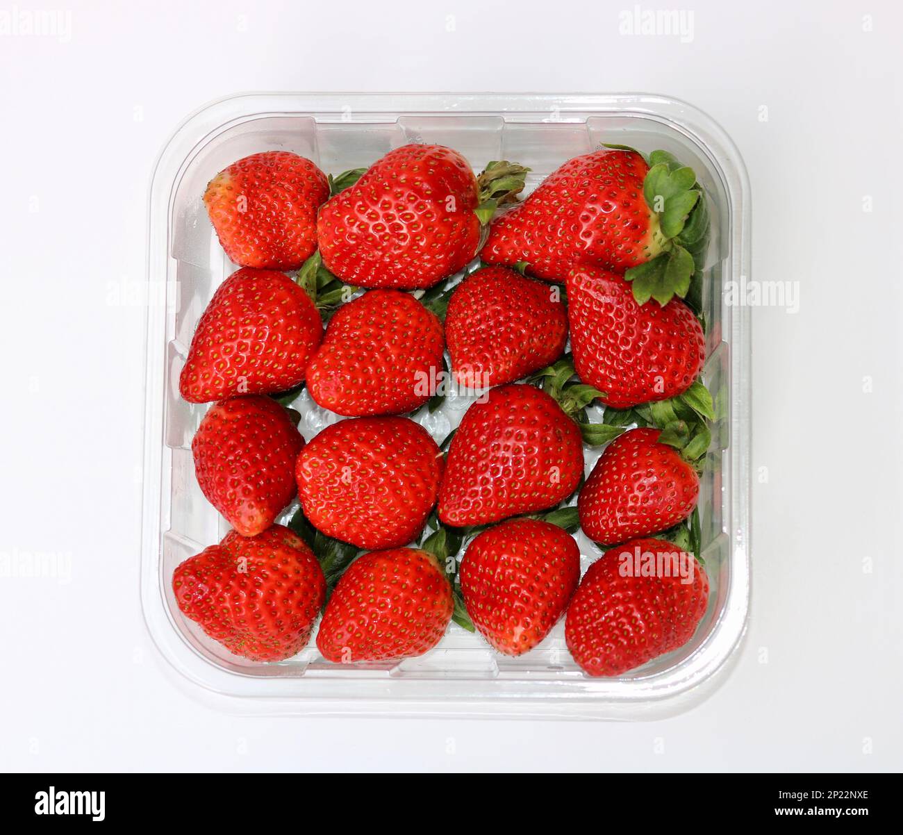Plastic punnet full of lush strawberries against plain white background ...