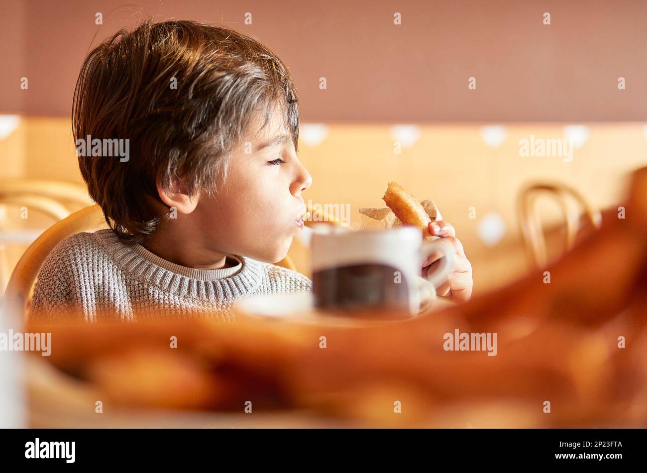 elementary age kid boy eating yummy churros into a hot chocolate mug ...