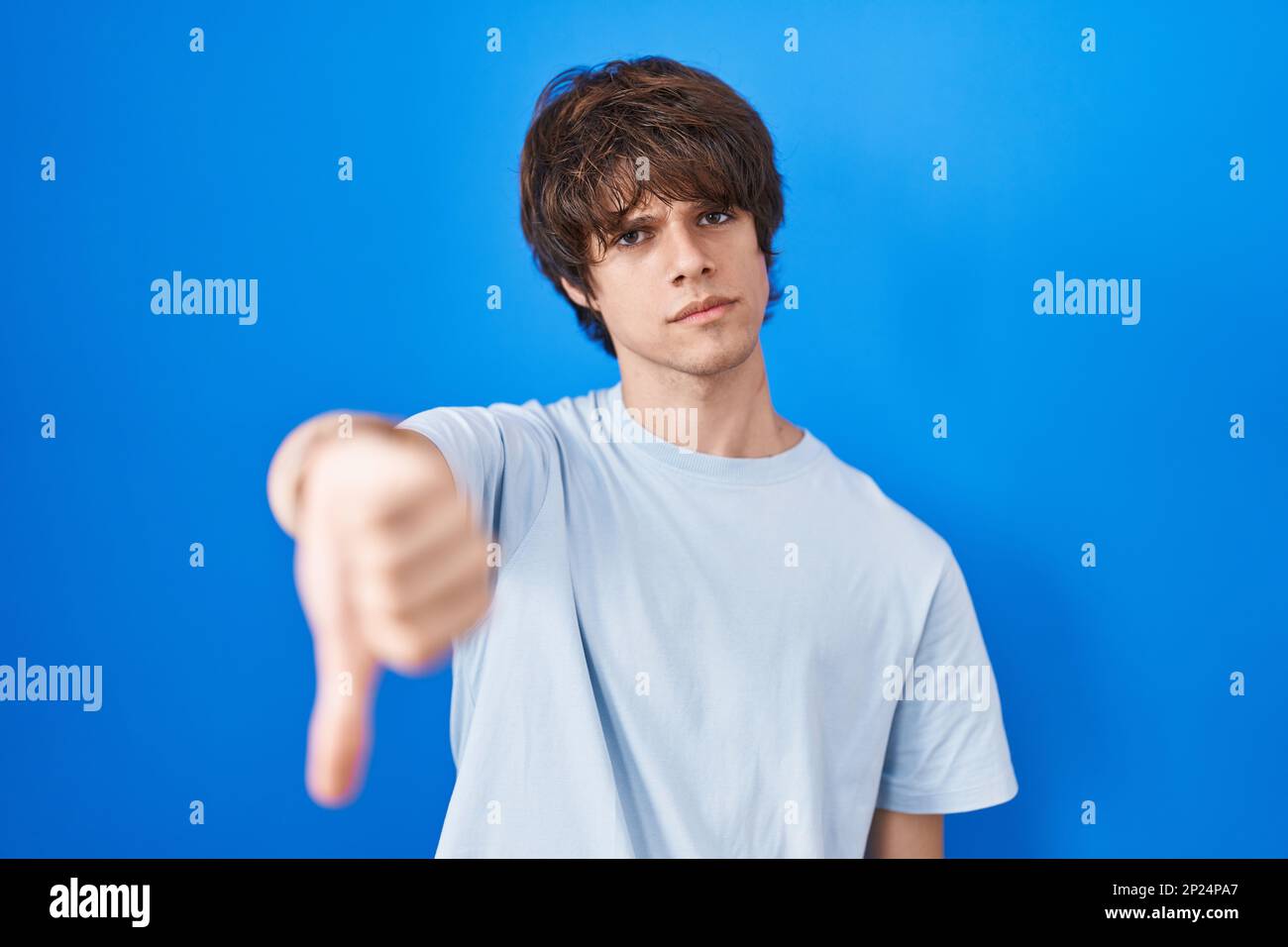 Hispanic young man standing over blue background looking unhappy and ...