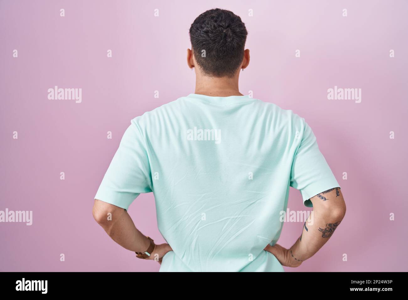 Handsome hispanic man standing over pink background standing backwards ...