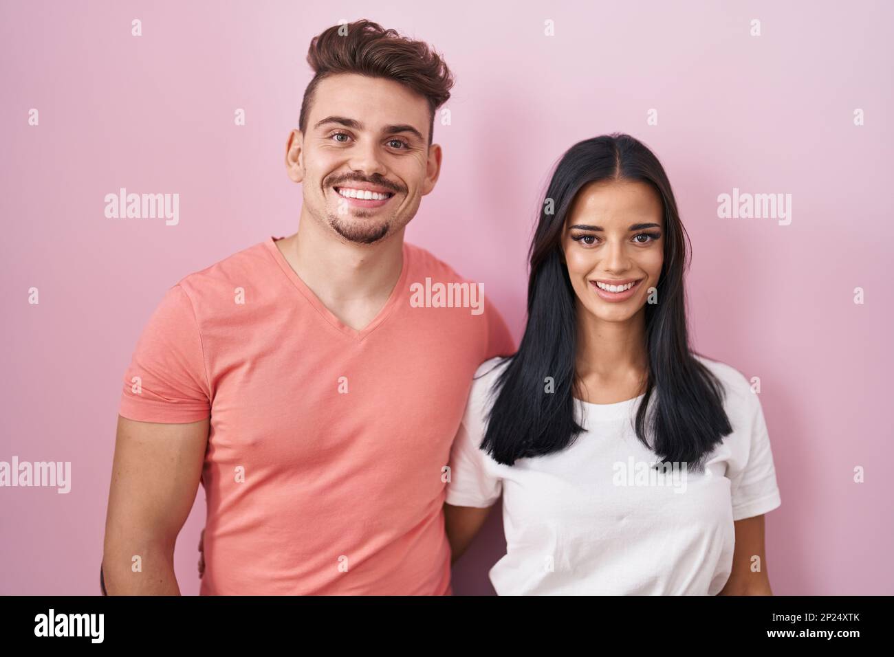 Young hispanic couple standing over pink background with a happy and ...