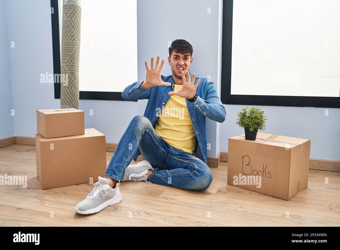 Young hispanic man sitting on the floor at new home afraid and ...