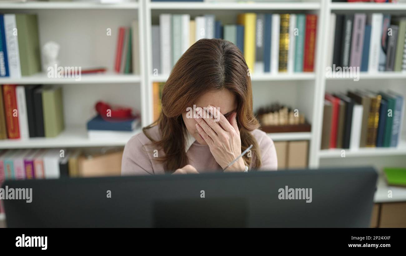 Young beautiful hispanic woman student using computer stressed at ...